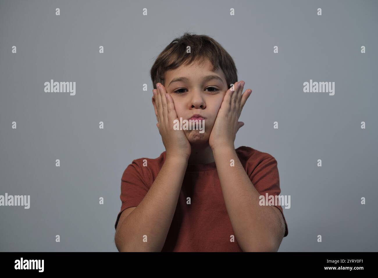 Boy puffing cheeks, hands framing face; a playful gesture. Captures the ...