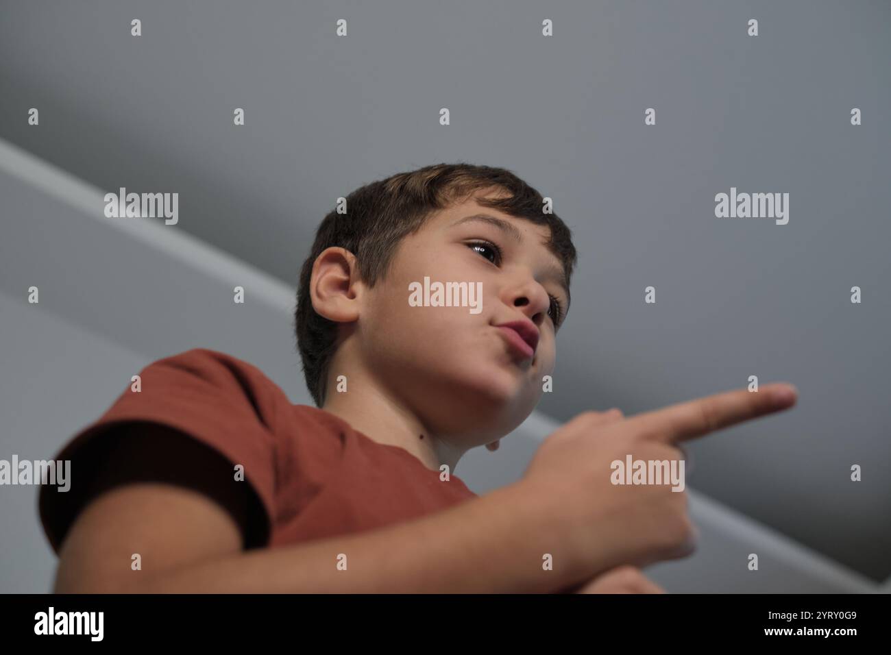 Young boy pointing upwards with a curious expression, shot from a low ...
