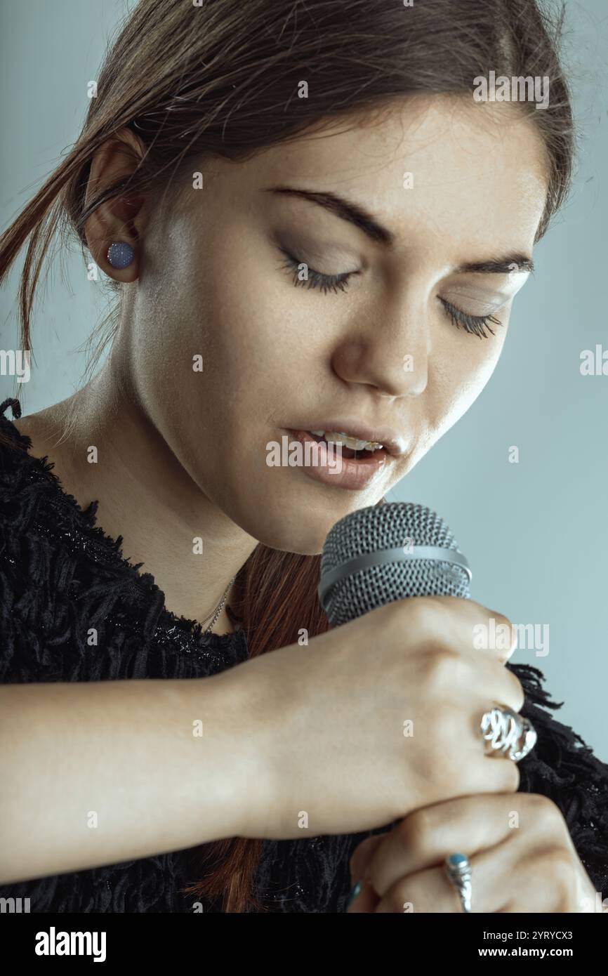 Young woman singing passionately into a microphone, eyes closed, fully ...
