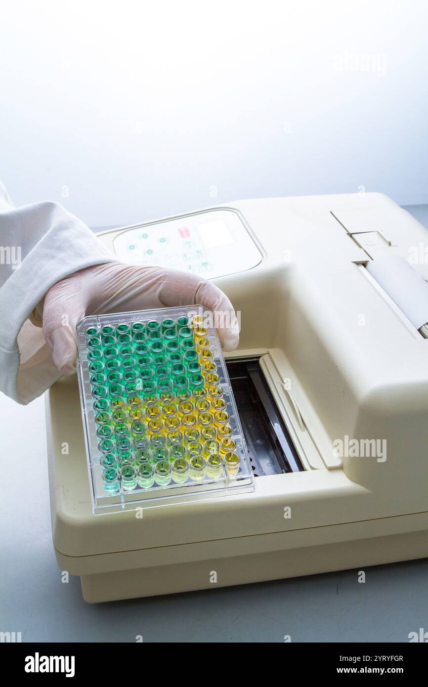 Gloved hand inserting microplate with green and yellow samples into ...