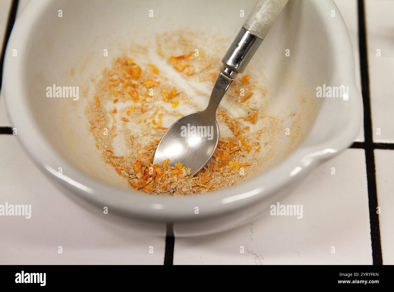 Mixing dried orange zest and powder in a white ceramic mortar using a ...