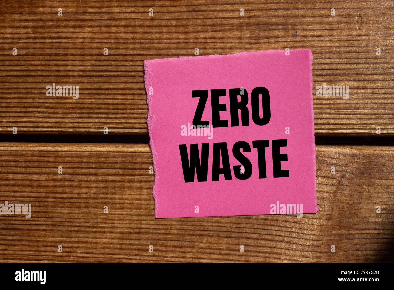Zero waste message written on ripped torn pink paper piece with wooden background. Conceptual ...
