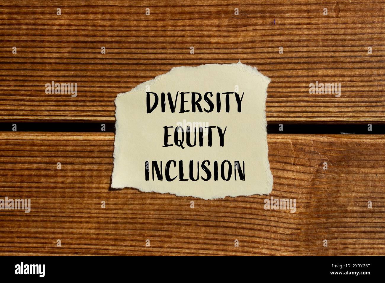 Diversity equity and inclusion message written on ripped torn paper with wooden background ...