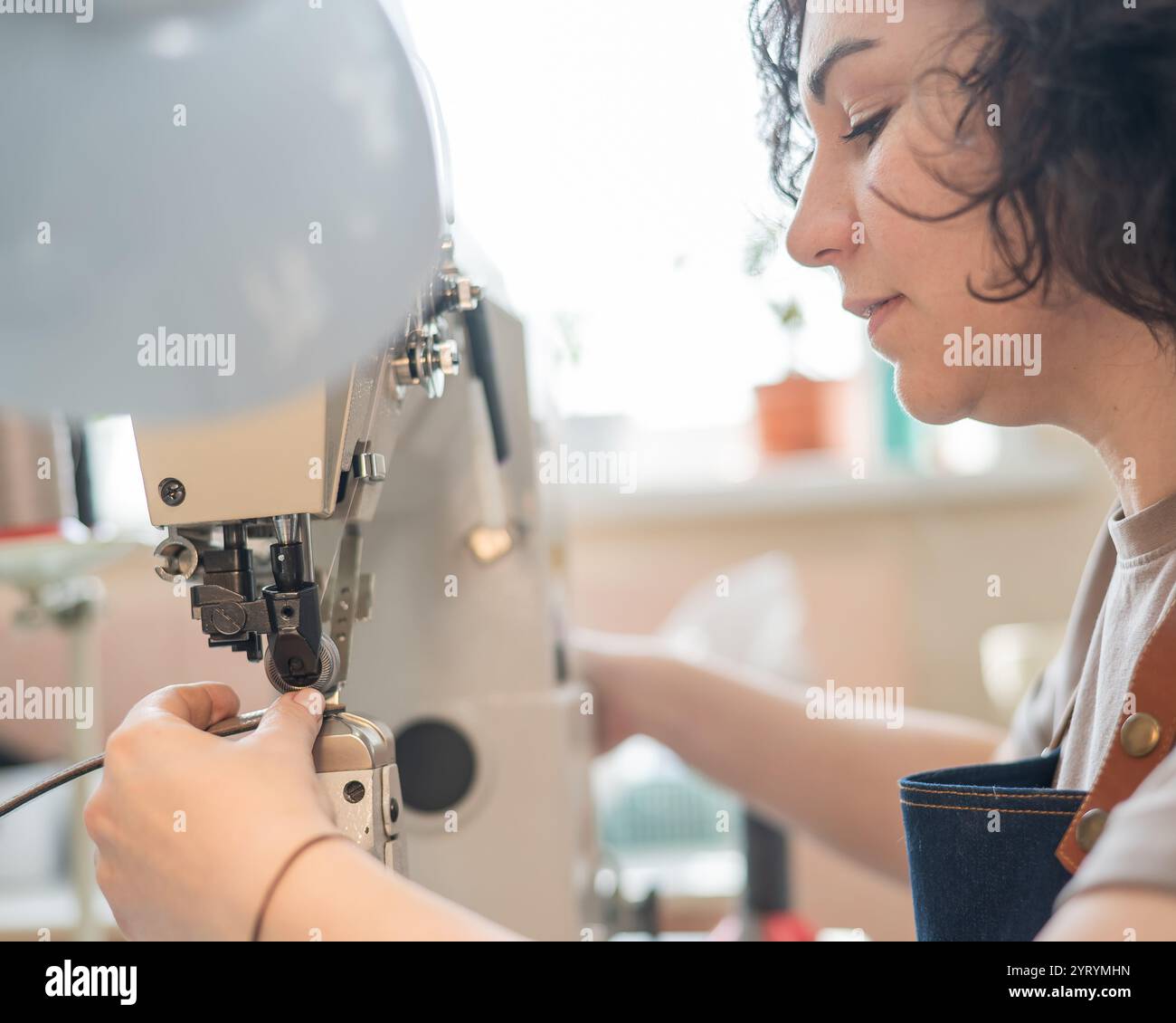 A woman tanner sews a leather belt on a sewing machine Stock Photo - Alamy