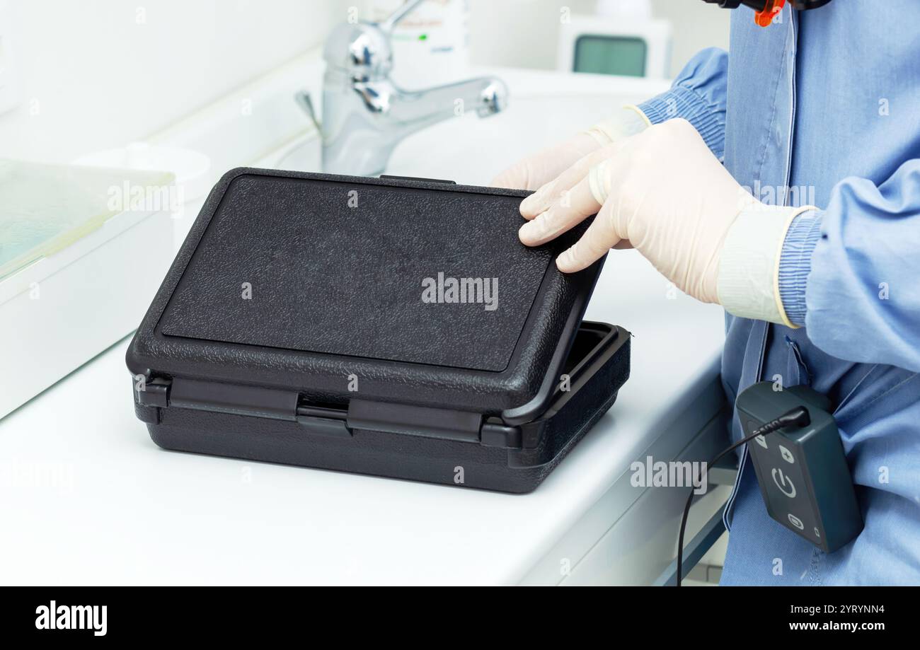 Dentist wearing gloves and opening a black sterilization box in a ...