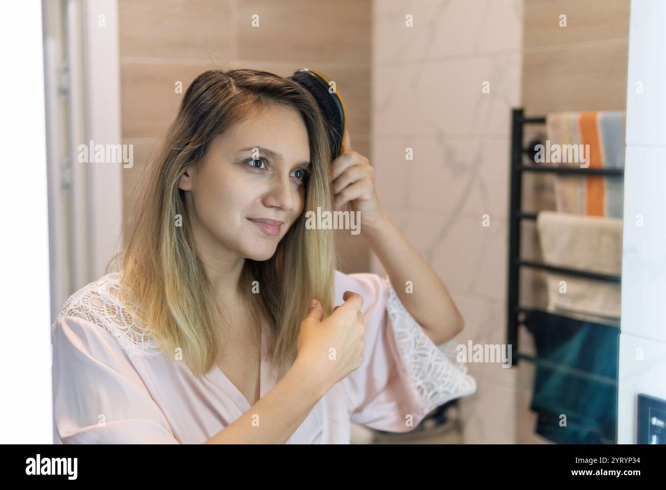 A woman is thoughtfully brushing her long hair in front of a beautiful ...