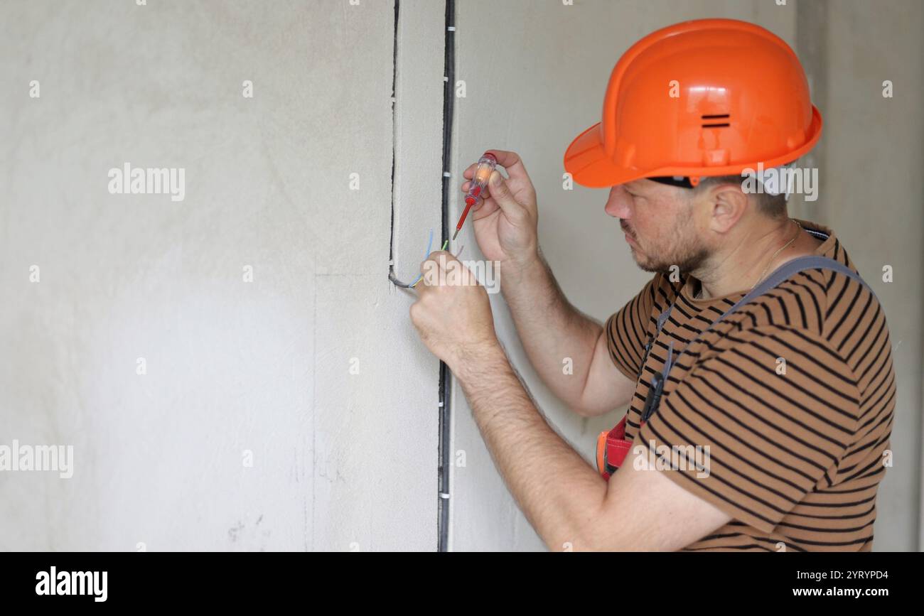 male electrician hands checks presence of electrical voltage in socket ...