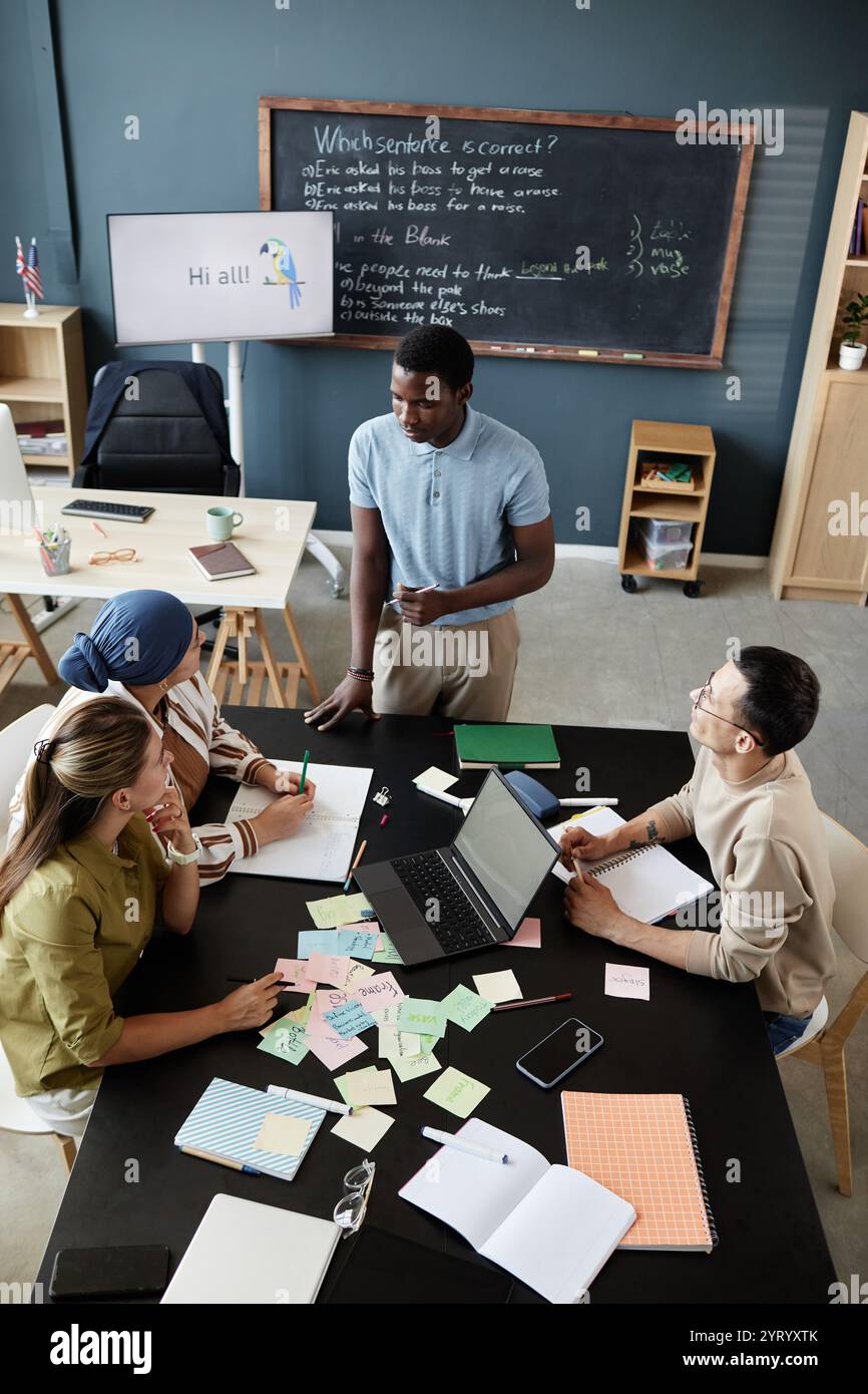 Vertical shot of young African American teacher standing at desk ...