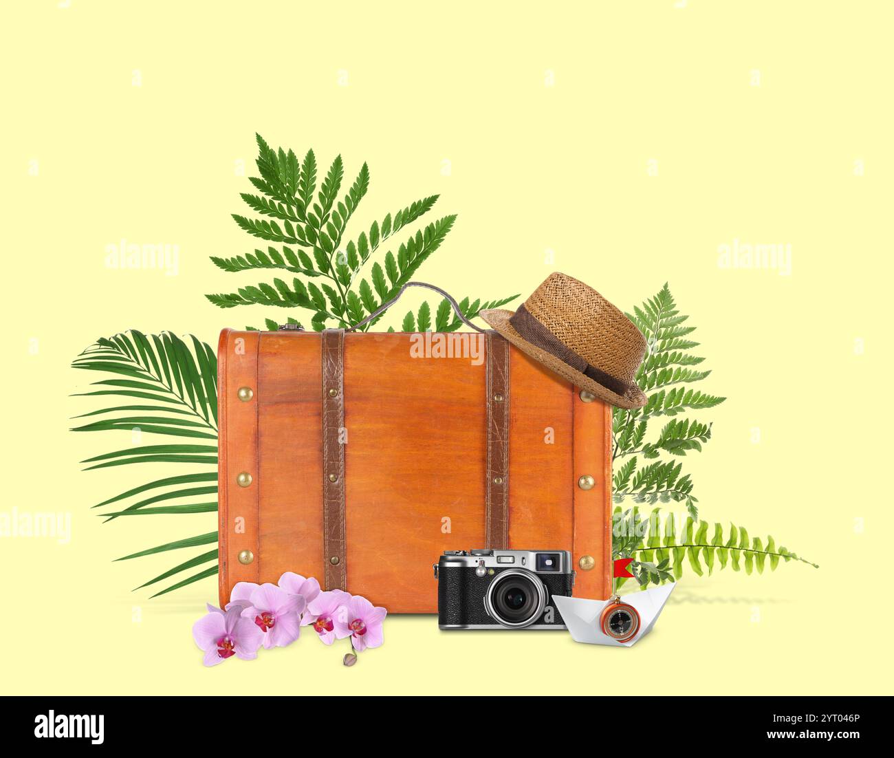 Brown travel suitcase, camera, paper boat, hat, tropical leaves and flowers on light yellow ...