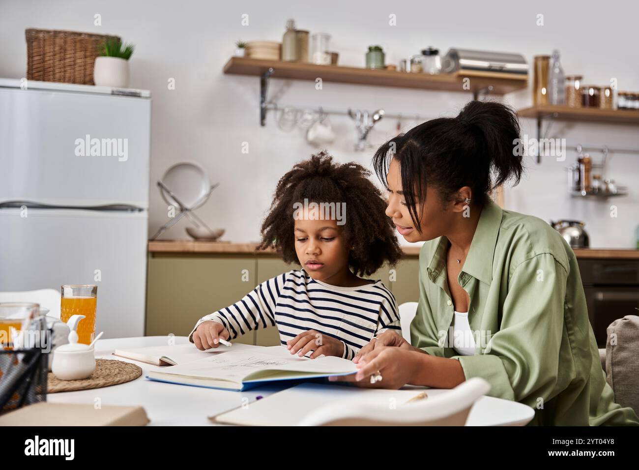 A devoted mother reads with her young daughter in their cozy kitchen ...