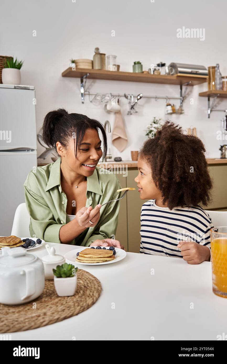A mother prepares pancakes while her daughter eagerly waits to taste ...