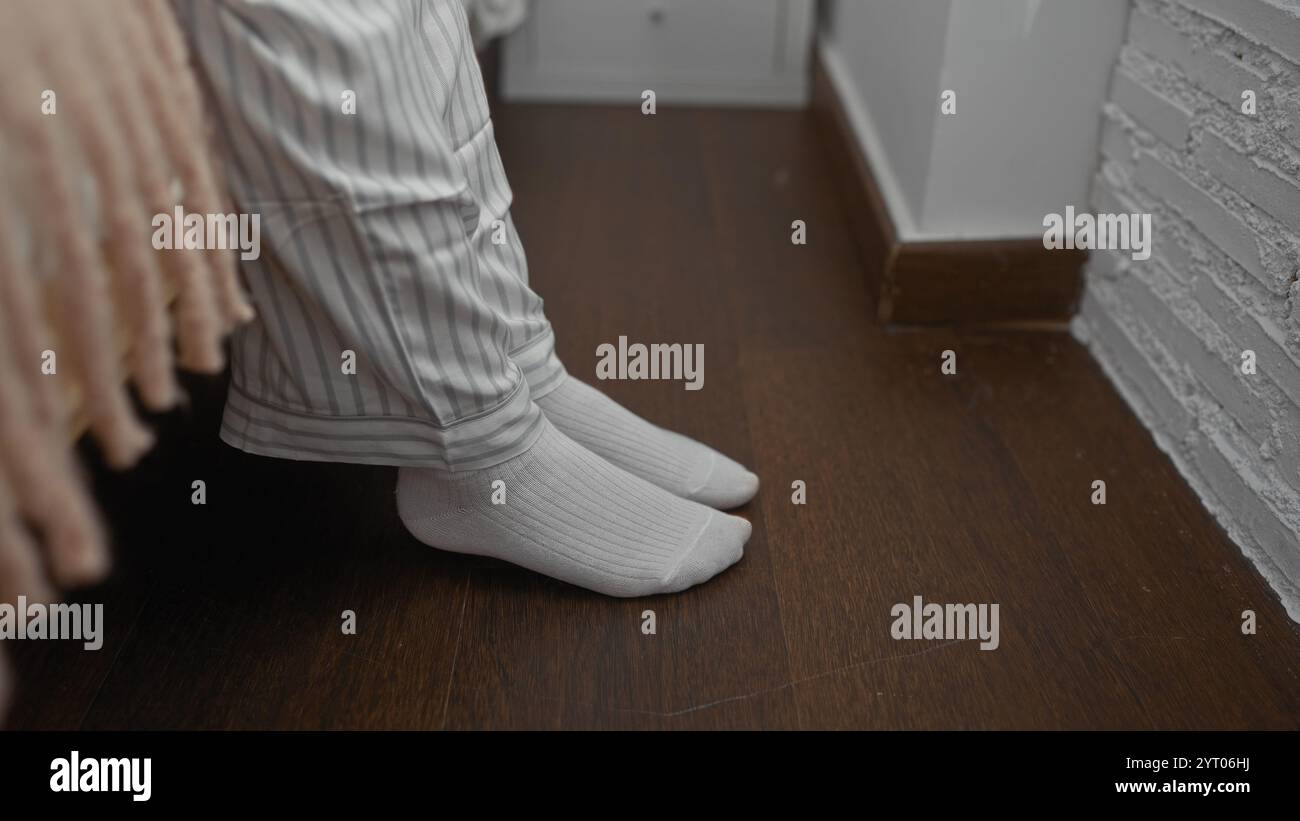Woman sitting on bed with socked feet touching wooden floor in cozy ...