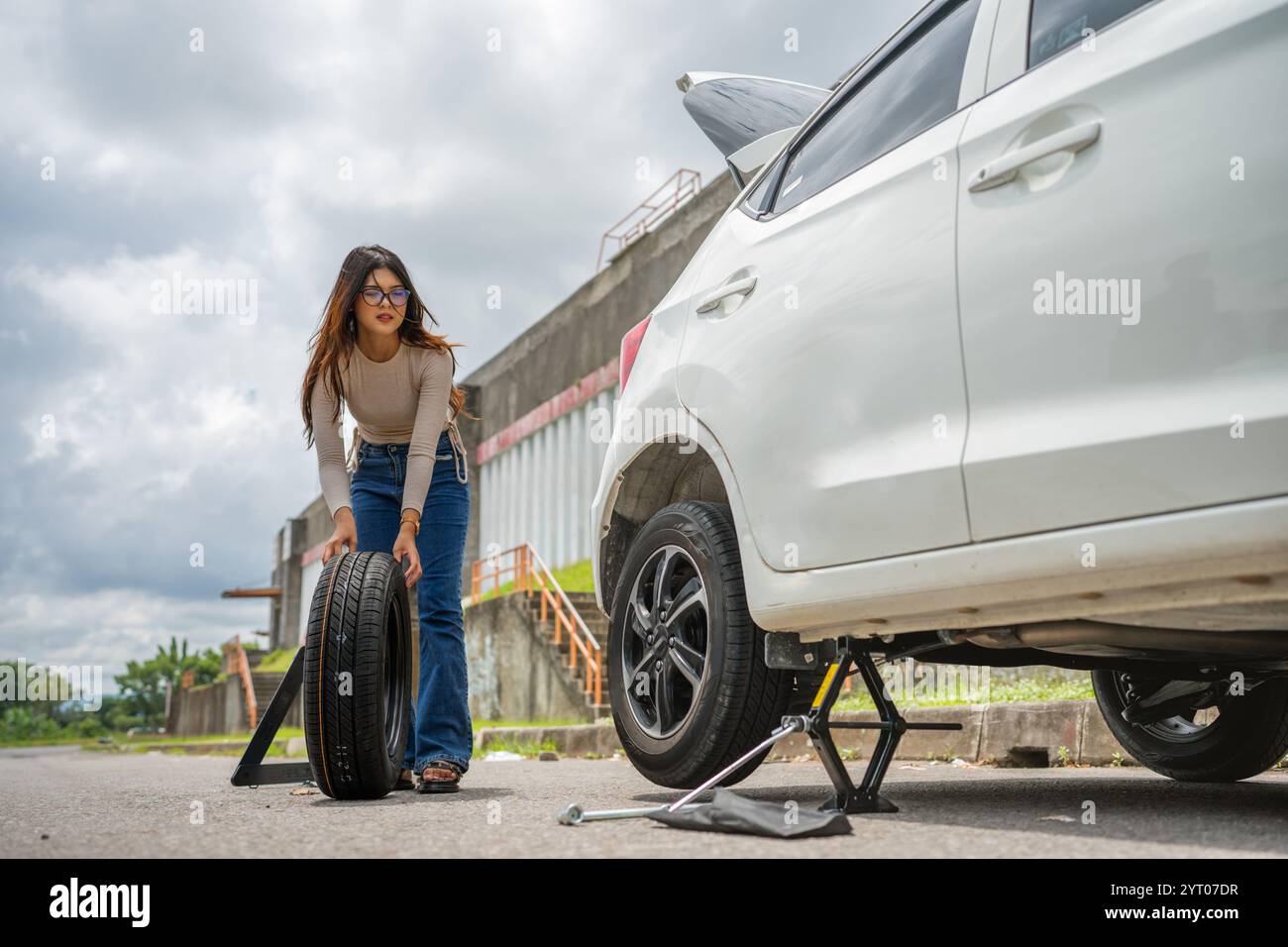 A woman is skillfully changing a tire on a white car in an outdoor ...