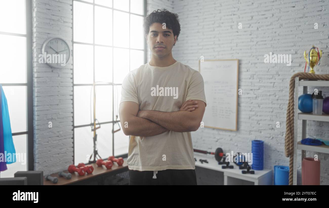 A handsome young hispanic man stands confidently in a modern gym with ...