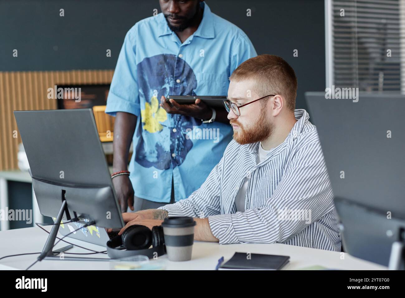 Two men working together at desk with computer equipment, discussing ...
