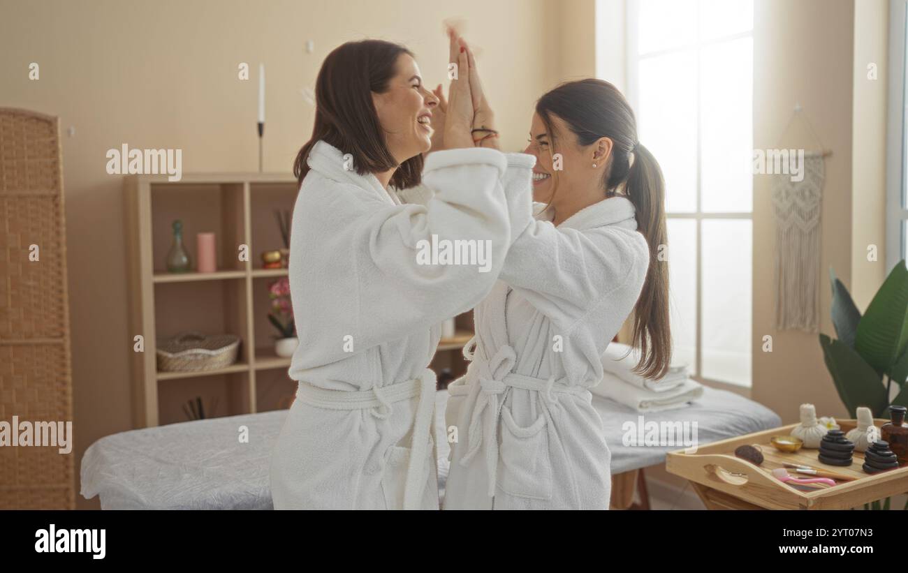 Two hispanic women joyfully celebrate together in a spa room, wearing ...