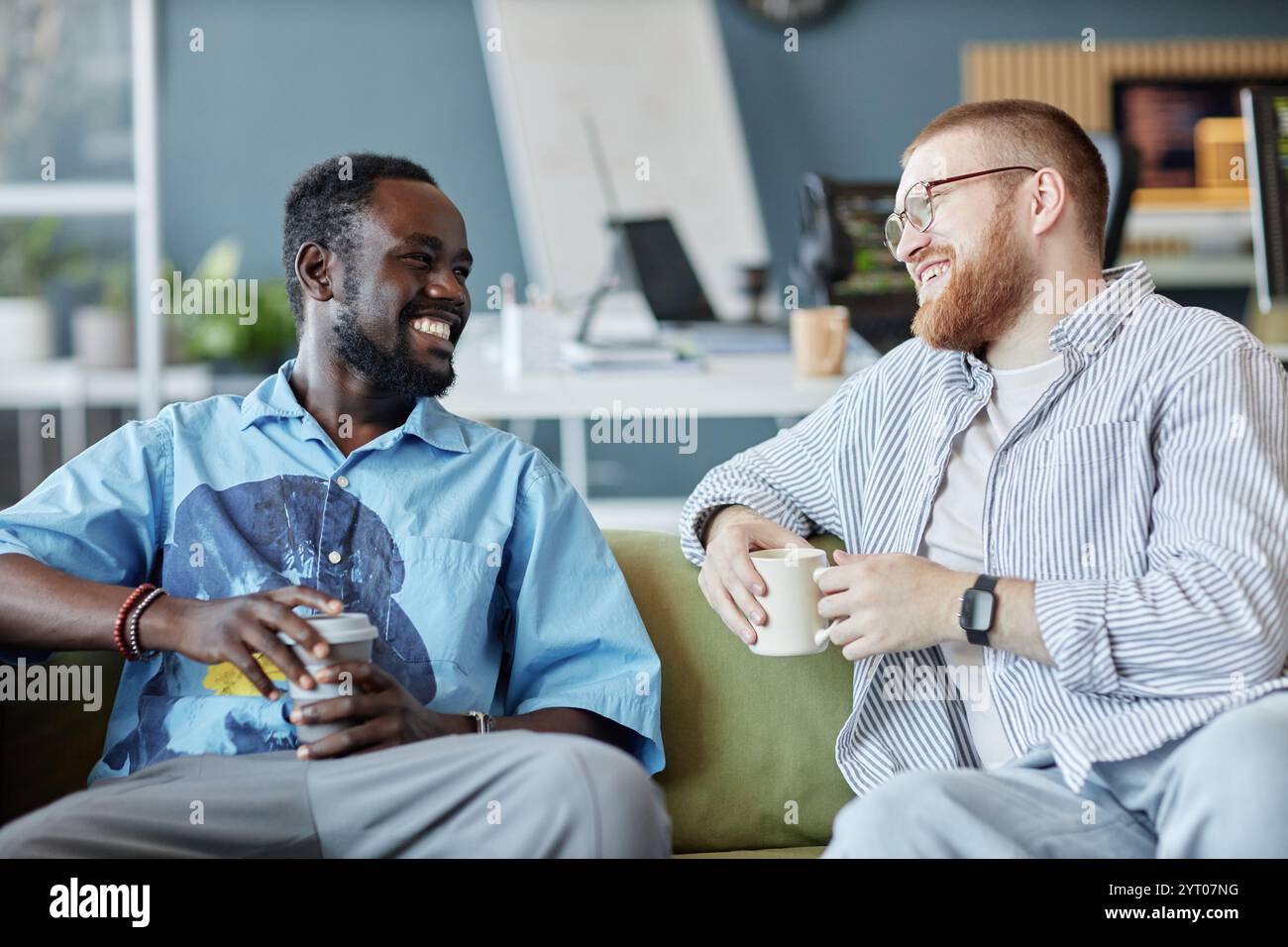 Two male friends enjoying coffee in bright office setting, sharing ...