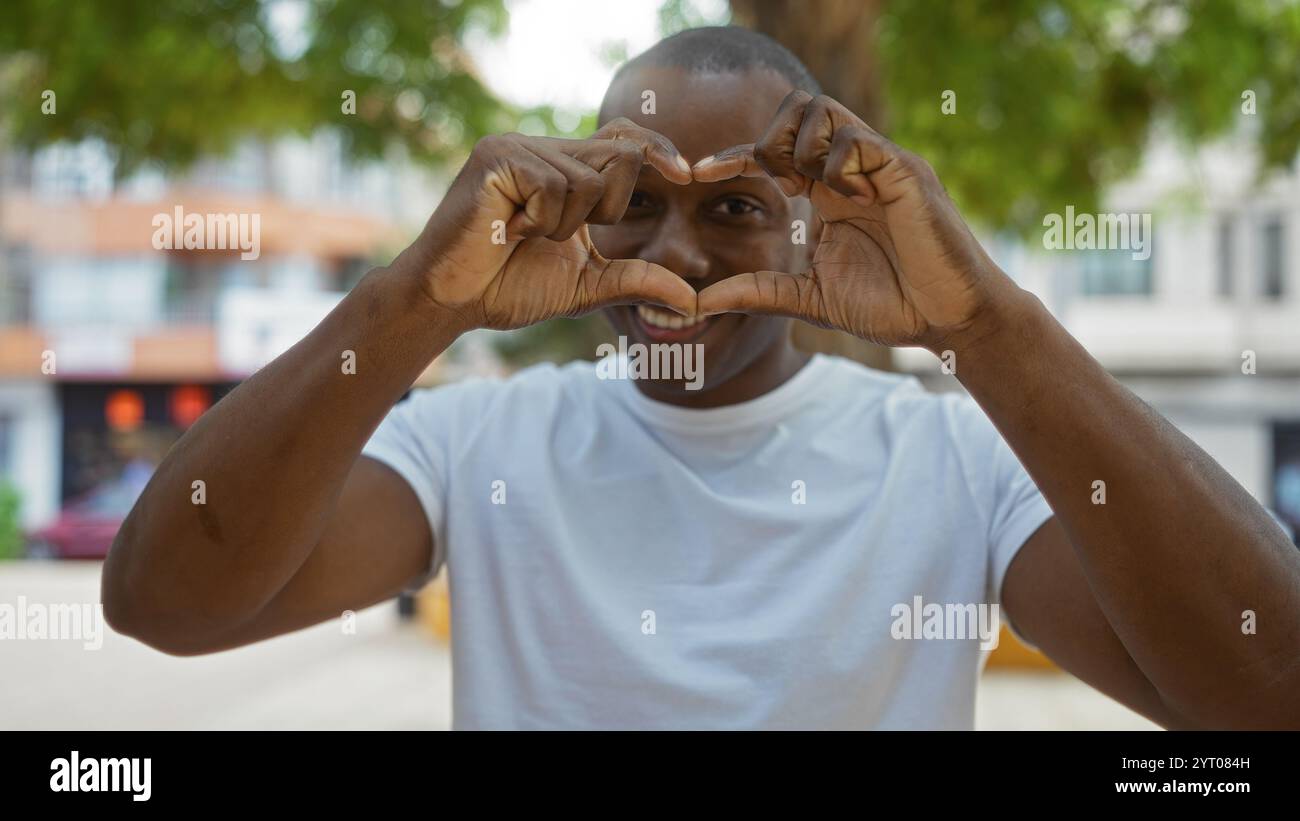 Young man smiling in urban park making heart gesture with hands ...