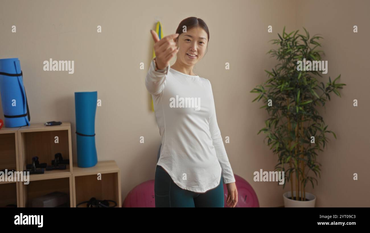 Woman smiling in a gym, showing playful gesture, surrounded by exercise ...