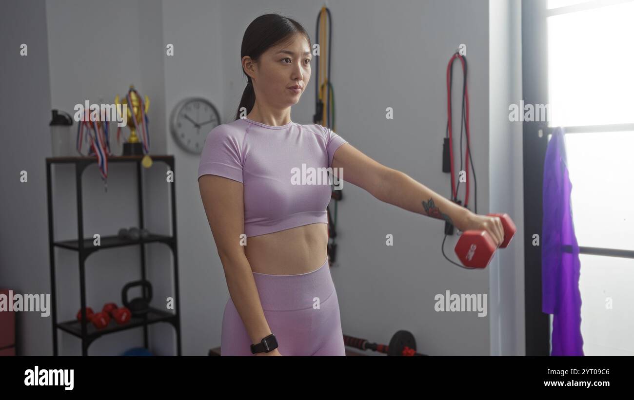 Young chinese woman exercising with a dumbbell in a gym filled with ...