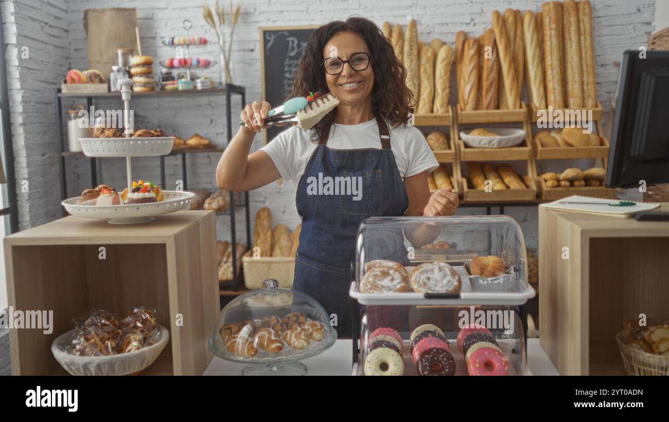 Woman smiling in bakery while holding pastry with tongs surrounded by ...