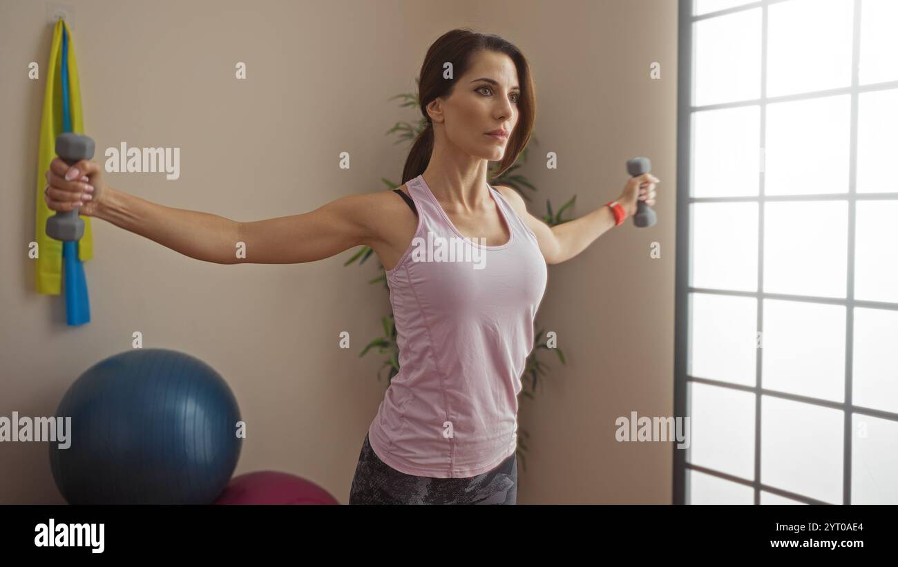 Woman exercising indoors holding dumbbells in a gym setting, showcasing ...