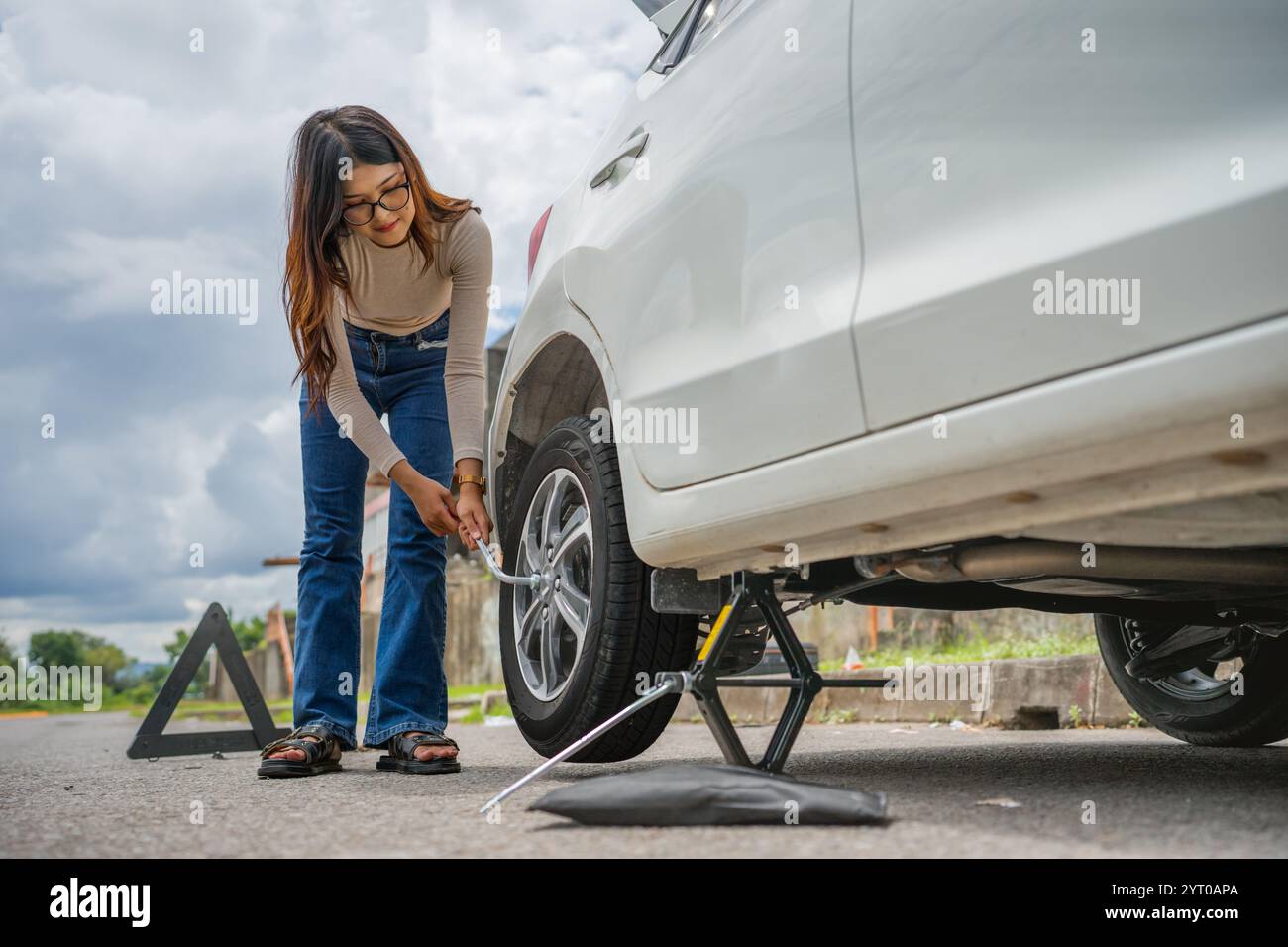 A woman diligently fixing a flat tire on a white SUV using a variety of ...