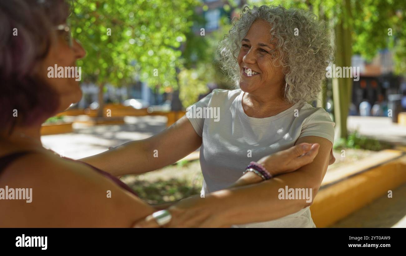 Two middle-aged women joyfully interacting outdoors with greenery ...