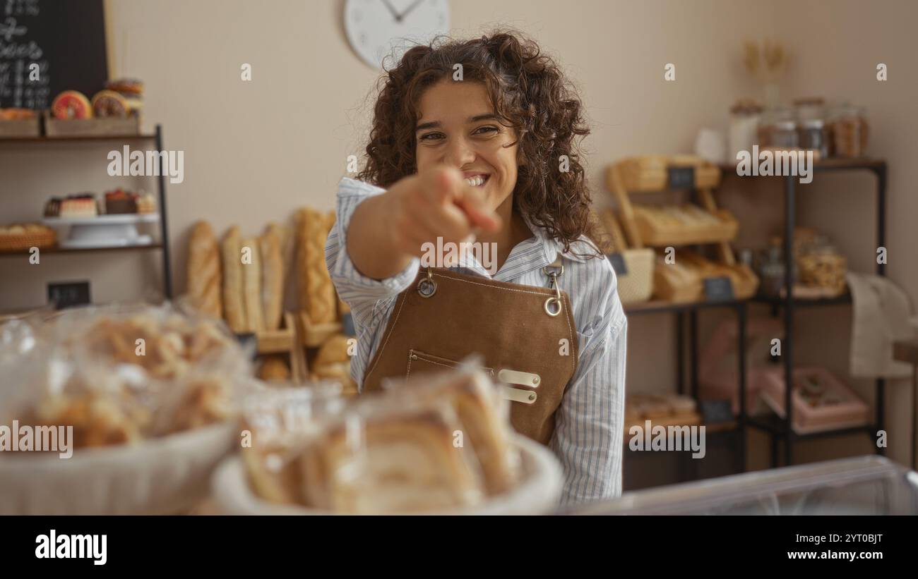 Young female baker smiling at the camera while pointing, surrounded by ...