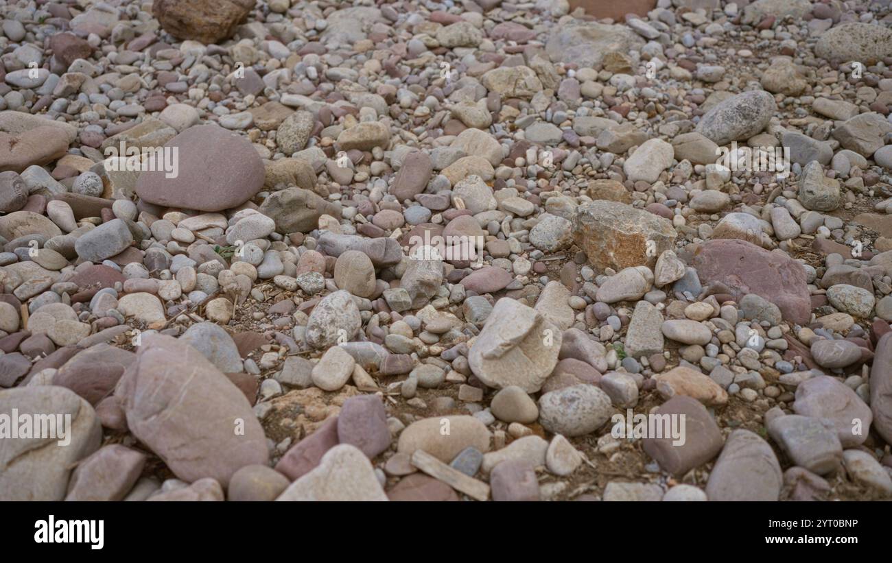Mixed-color pebbles and rocks scattered across a dry riverbed in an ...