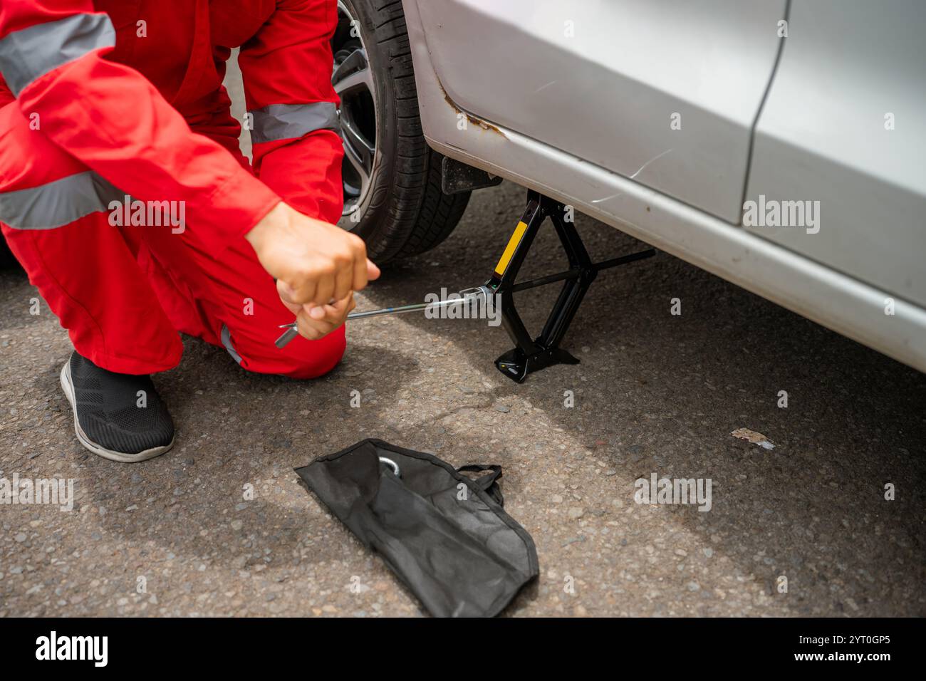 A mechanic dressed in a red uniform is changing a tire using a jack on ...