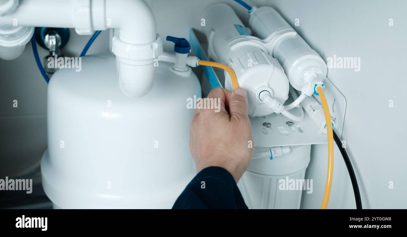 a caucasian man, wearing blue overalls, is installing a reverse osmosis ...
