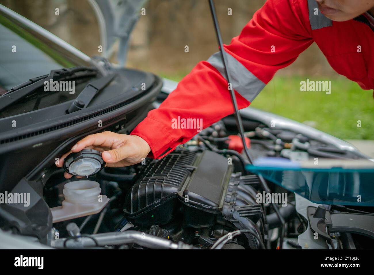 A mechanic is checking the engine coolant level under the hood of a car ...