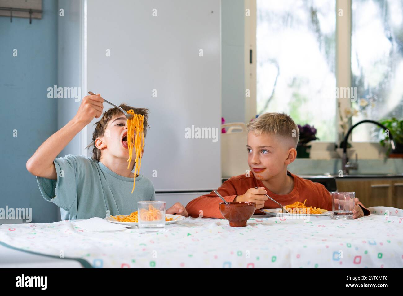 Two brothers enjoying a spaghetti meal, one playfully slurping a long ...