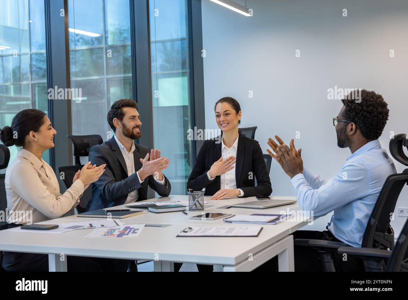 A diverse group of professionals is seen applauding during a successful business meeting. The ...