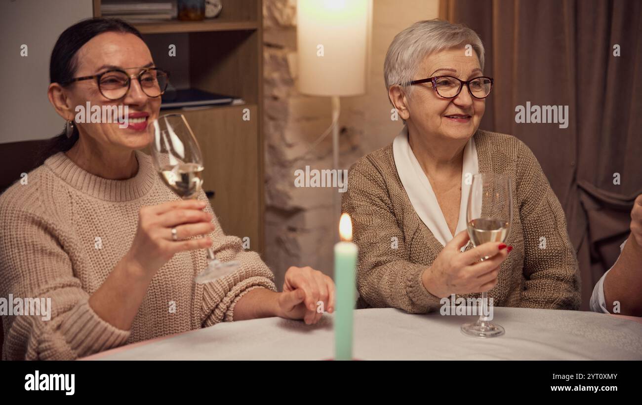 Two women dressed in cozy warm sweaters, sitting at table in warmly lit ...