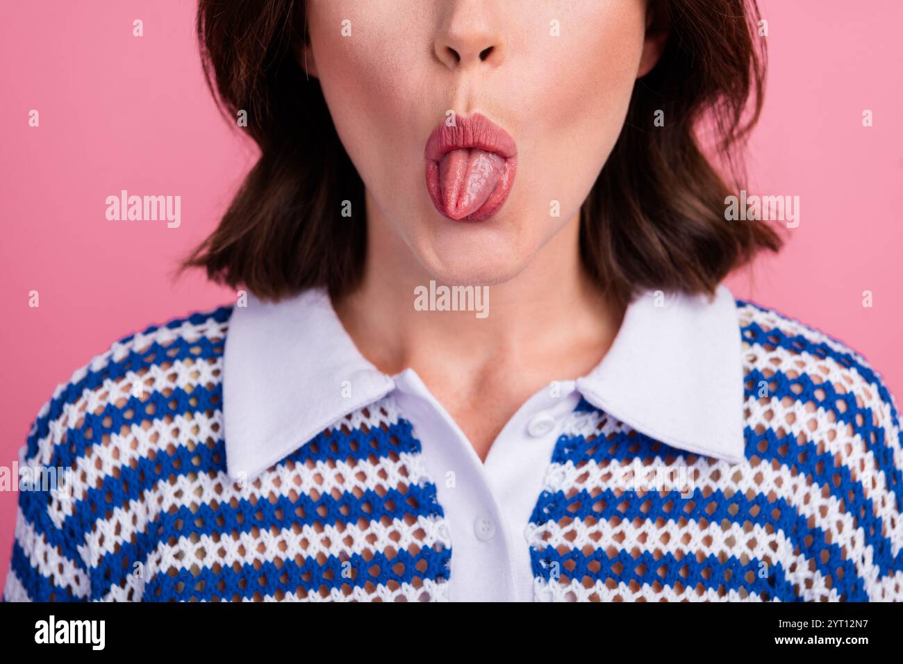 Young woman in trendy striped knit top playfully sticking out tongue ...