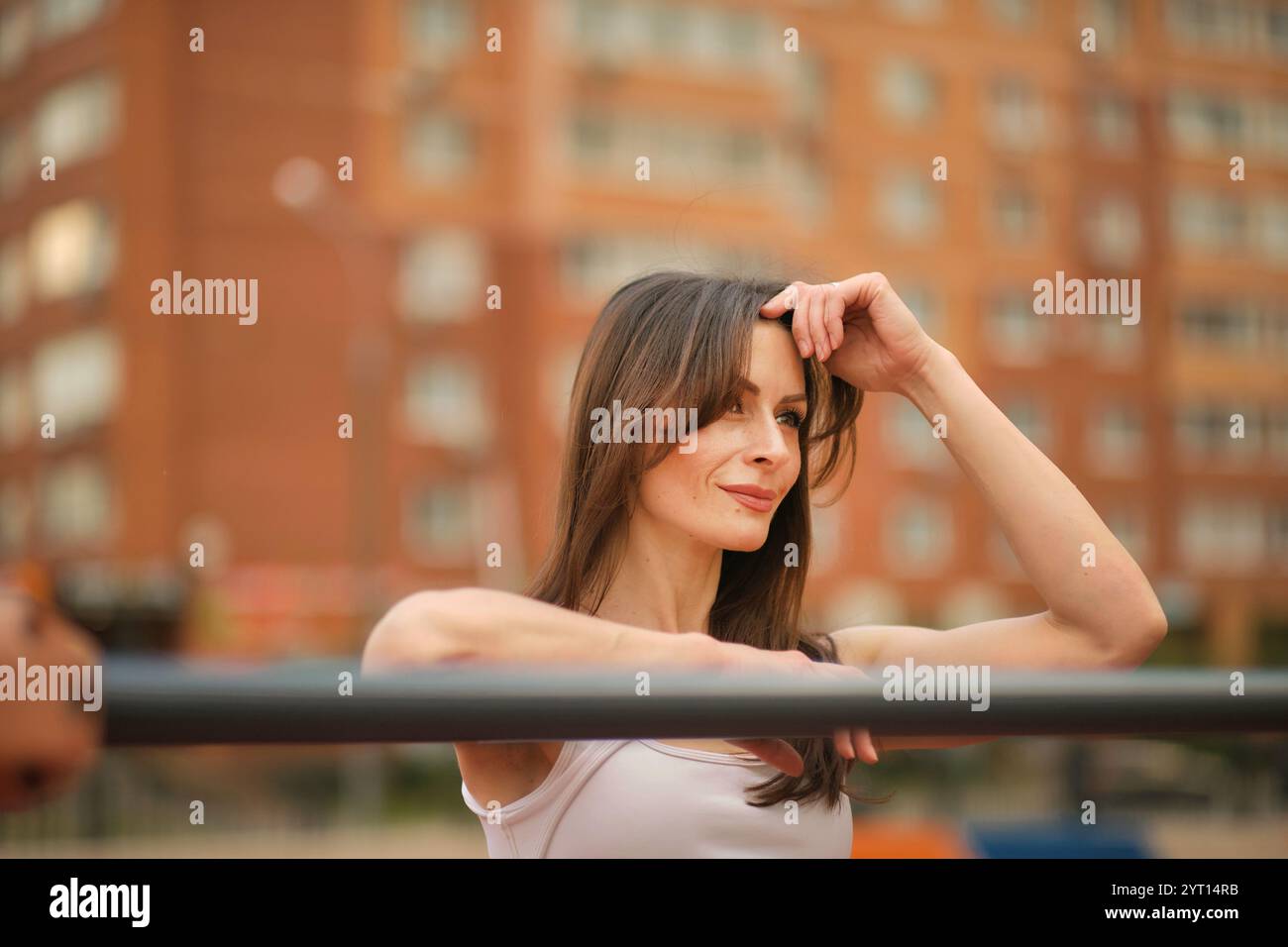 A fit woman smiles while leaning on gym bars, her relaxed posture ...