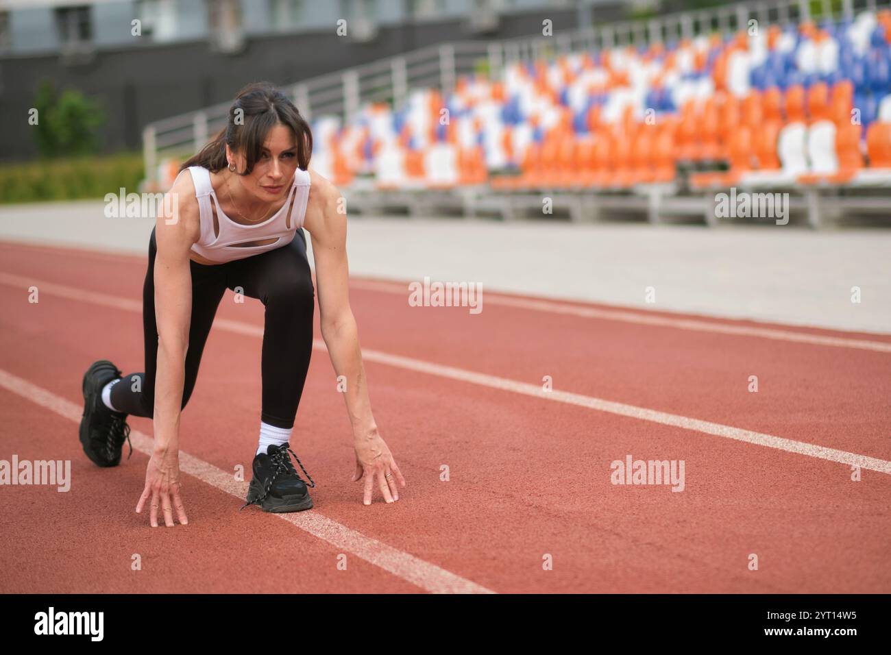The athletic woman prepares to start a race on the track, her focused ...
