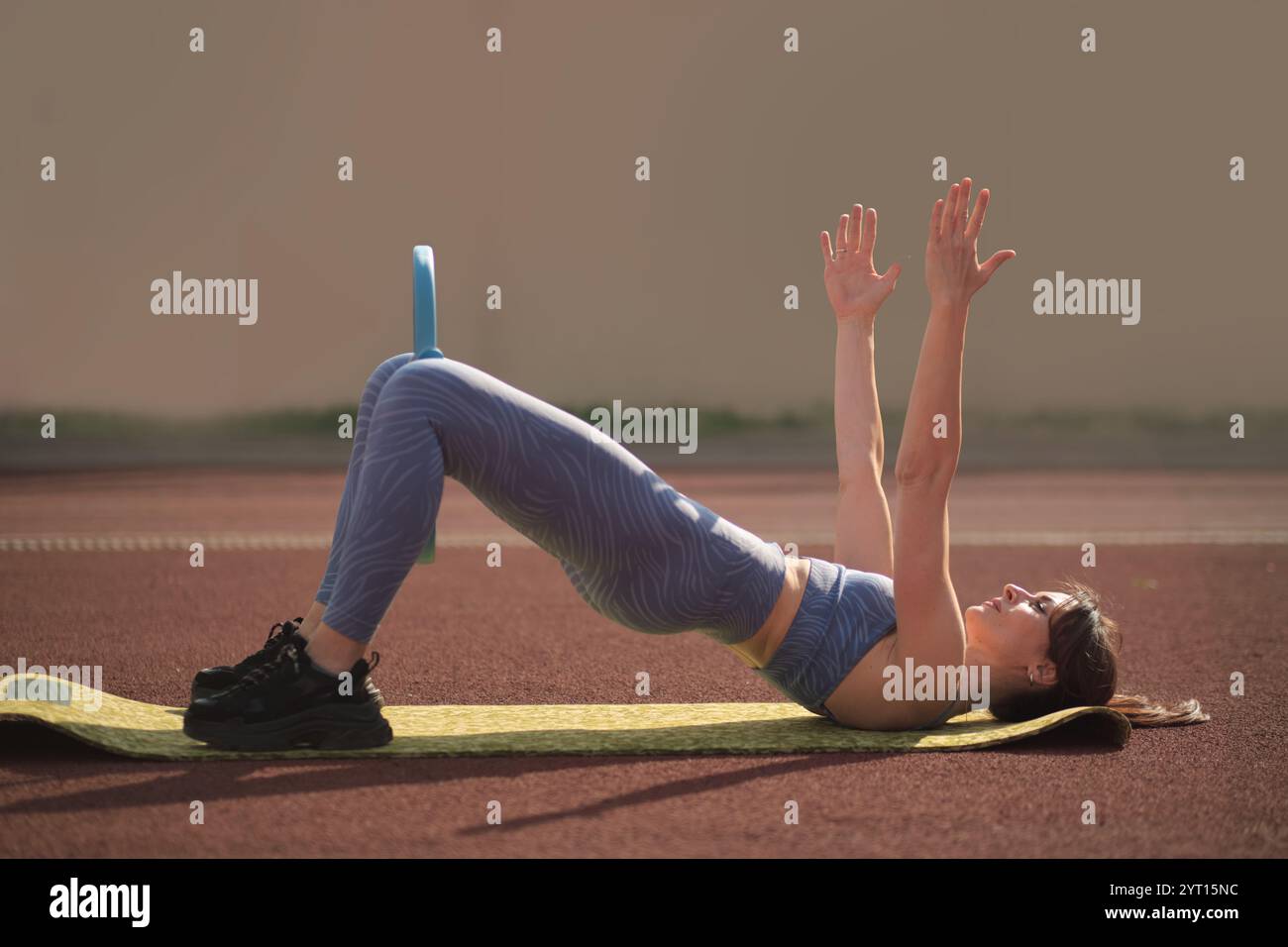 Lying on a mat, the woman engages in a bridge pose using a fitness ring ...