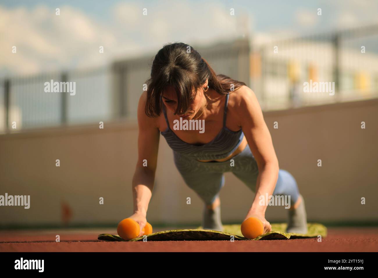 yellow mat, the woman in blue sports attire holds a plank with weights ...