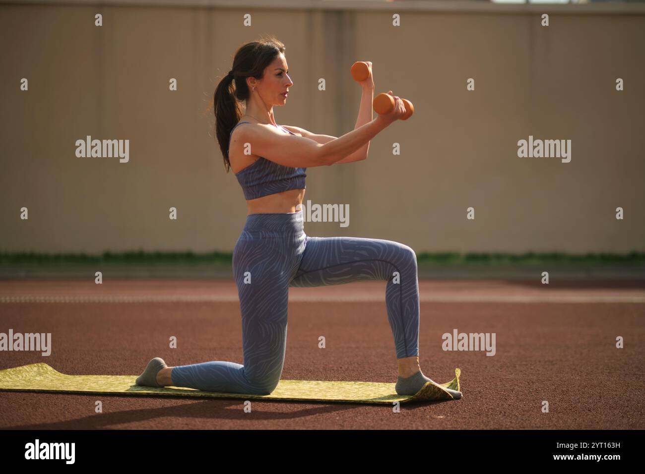 woman in blue sportswear performs a lunge exercise with dumbbells on a ...