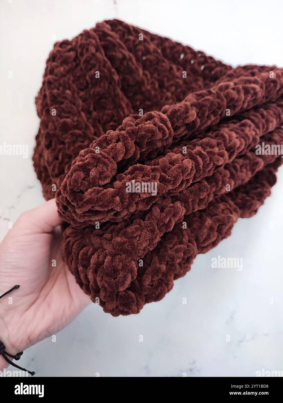 Knitted hat in hand, dark brown chocolate beanie hats on white marble ...