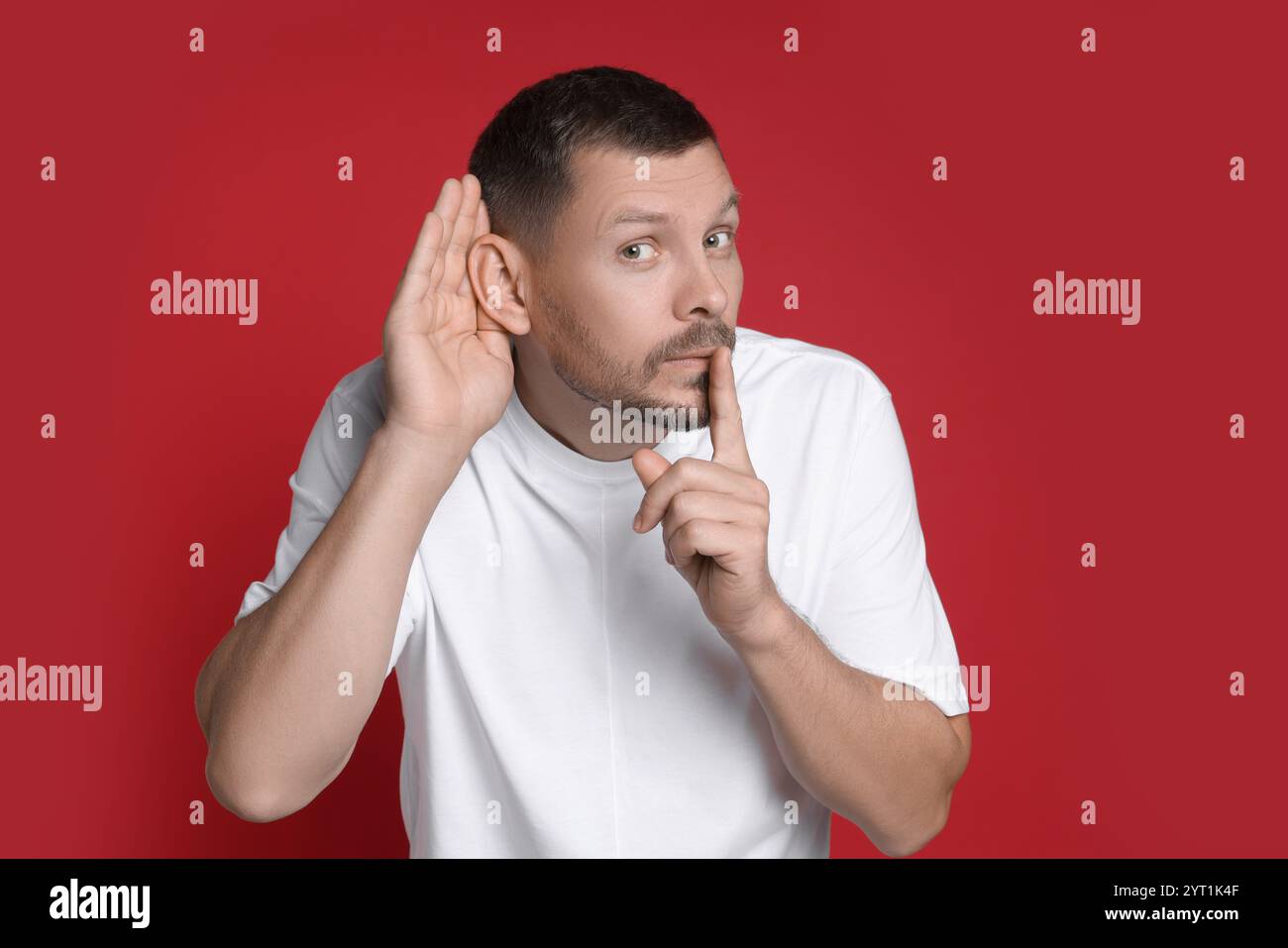 Man showing hand to ear gesture on red background Stock Photo - Alamy