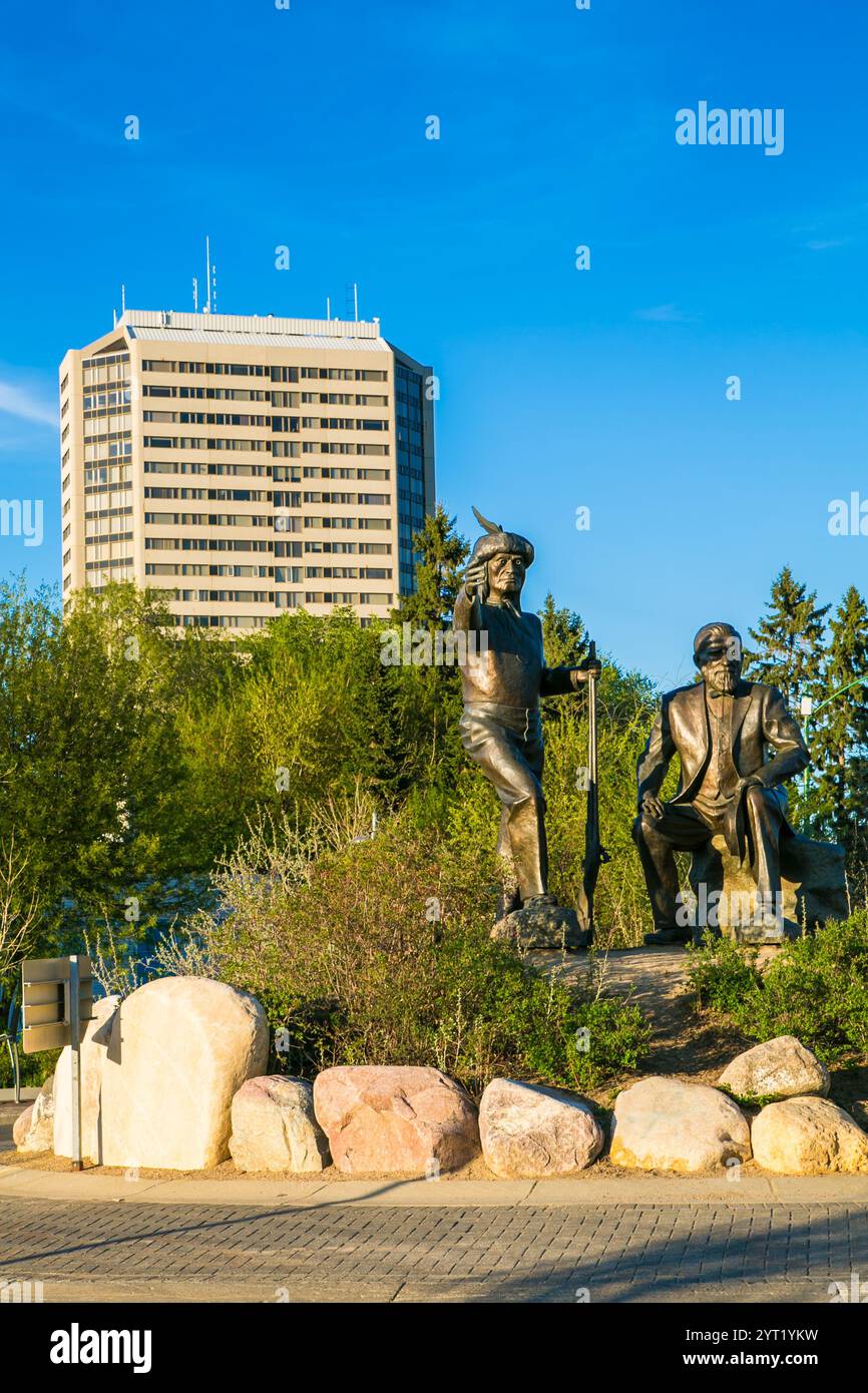 A statue of two men sitting on a rock in front of a large building. The ...