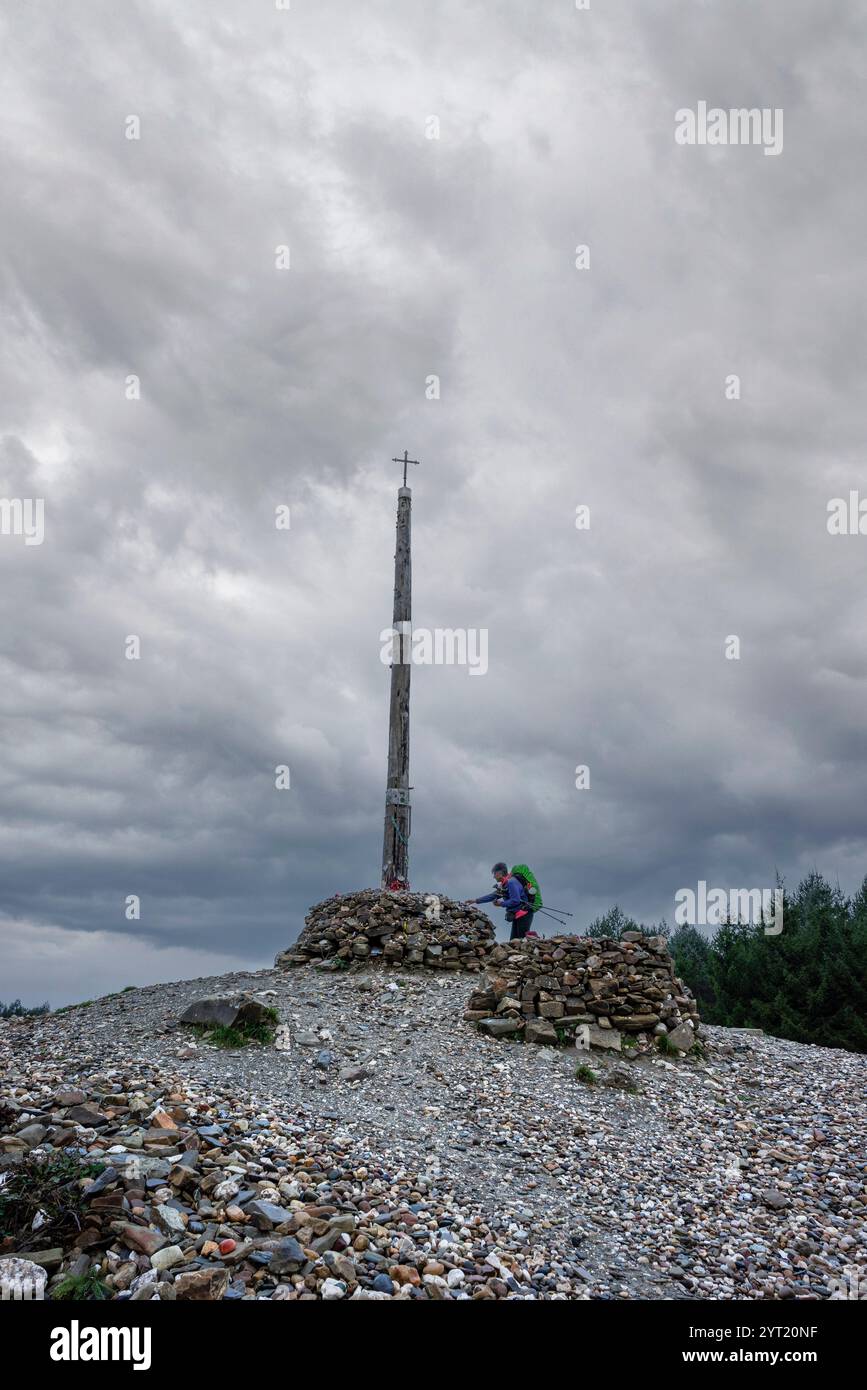 Pilgrim on the Camino de Santiago offering votive stones and offerings in Cruz de Ferro (Iron ...