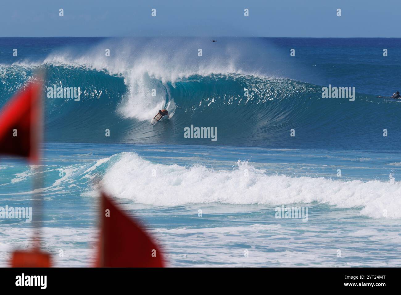 Nov 30 2024, Pupukea, Hawaii. A surfer drops into a wave with red high surf warning flags on the ...