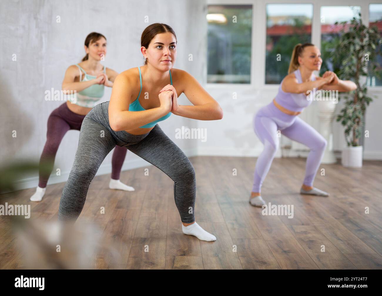 Inspired young fit women in tight sports clothes doing squats during ...