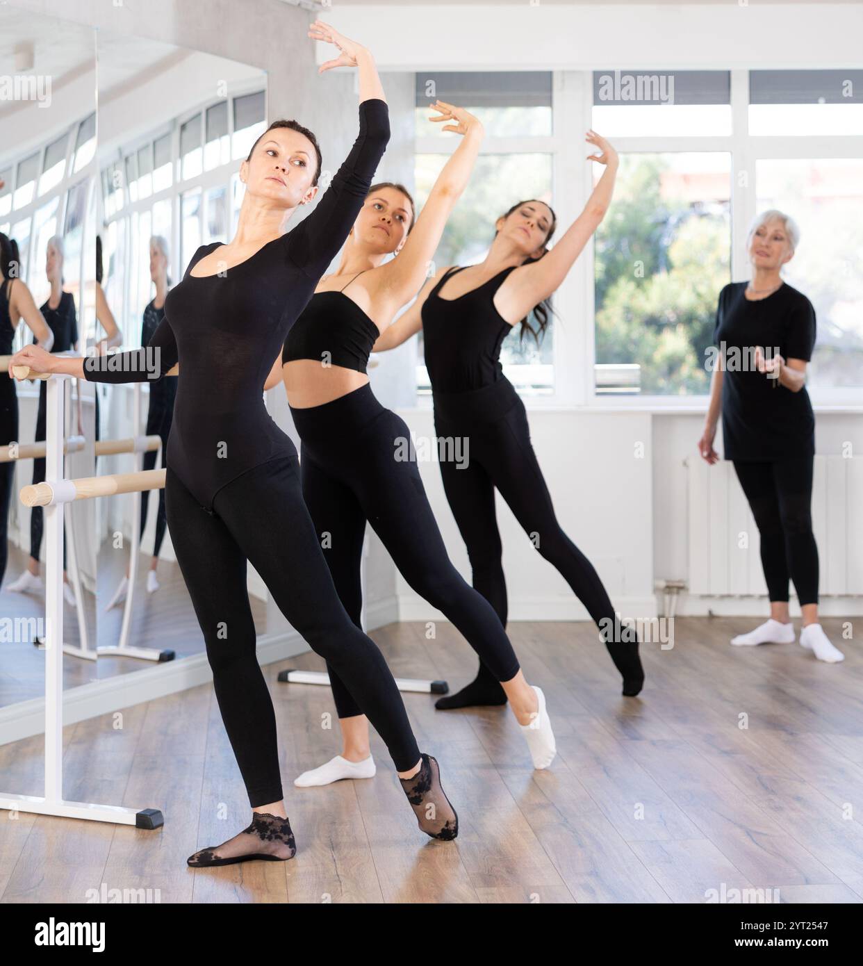 Female ballet trainer teaching group of dancers near ballet barre in ...