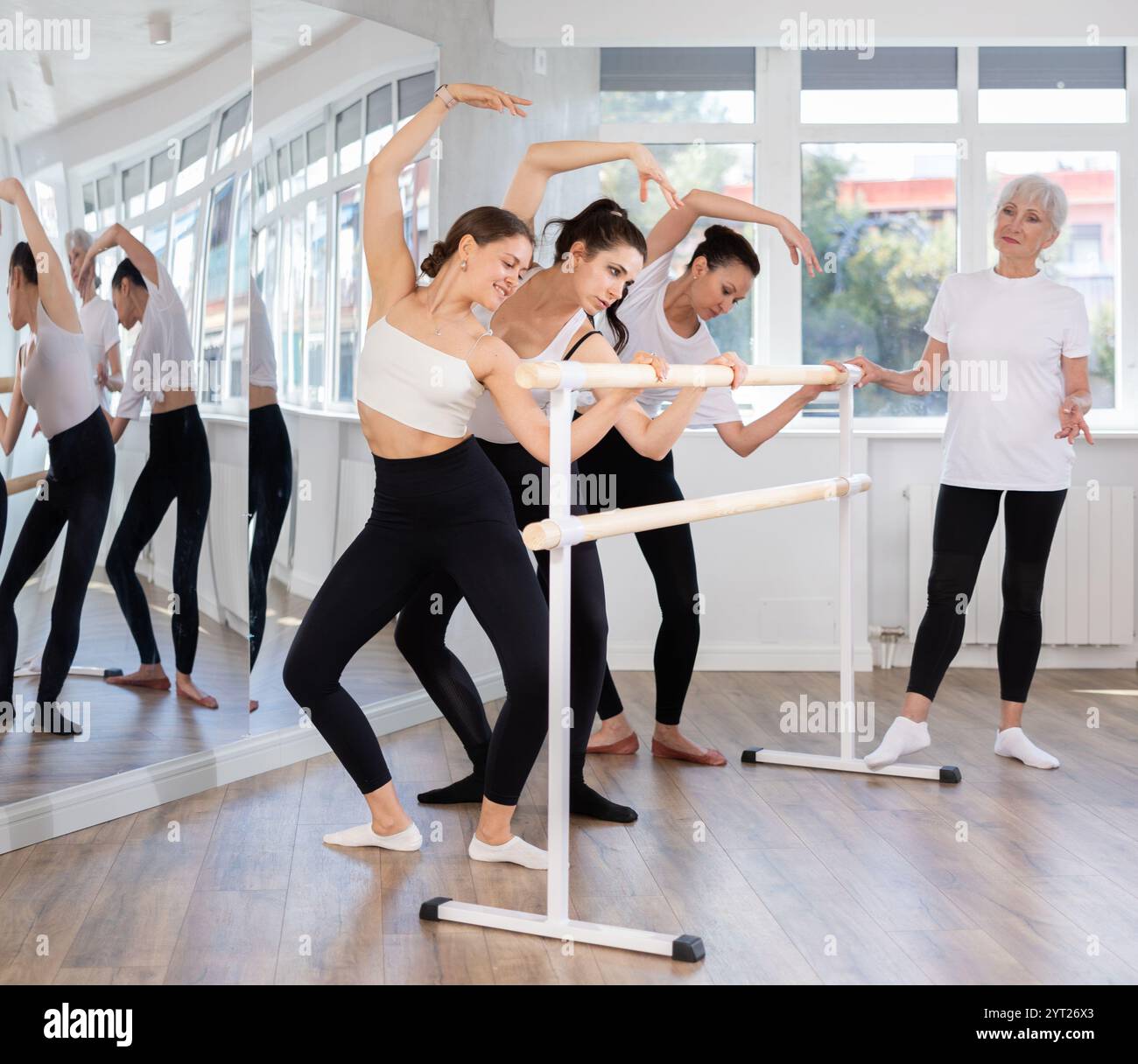 Young woman performing demi plie with cambre at barre in ballet class ...